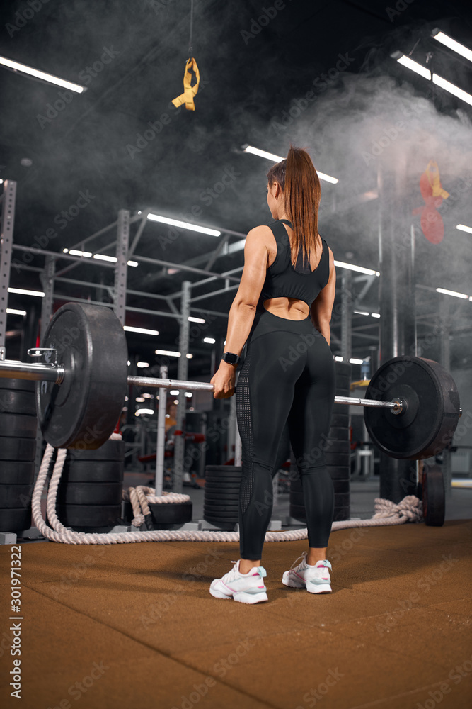 Strong tall female bodybuilder preparing to lift heavy barbell up ...