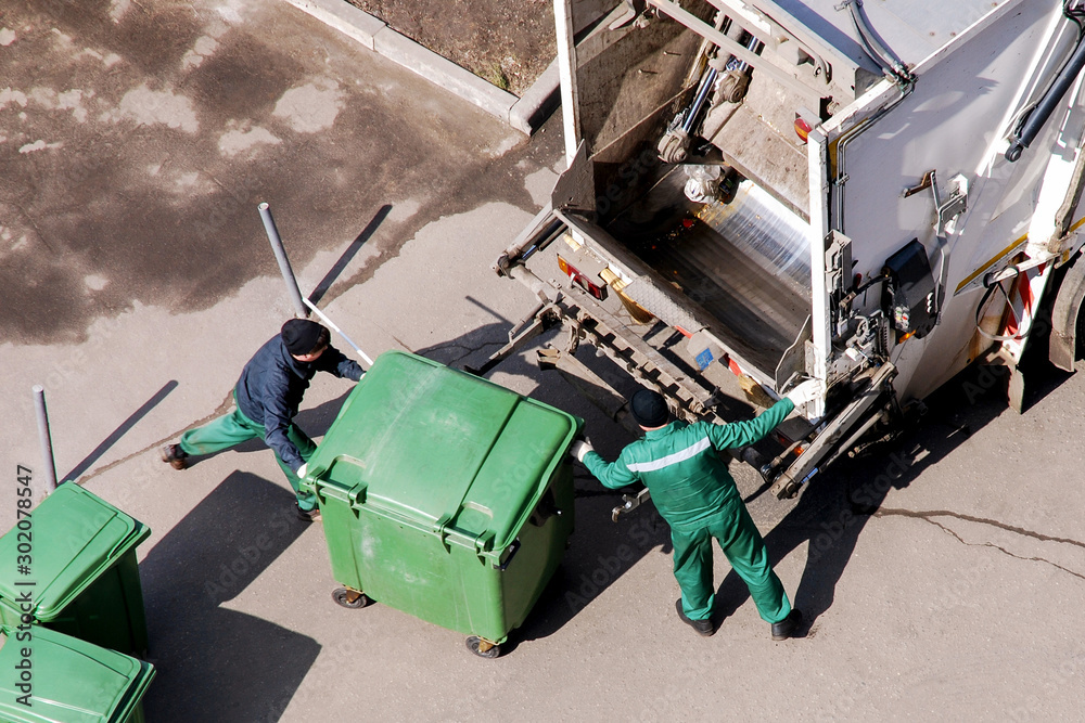 Garbage collection workers in residential area operating garbage truck ...