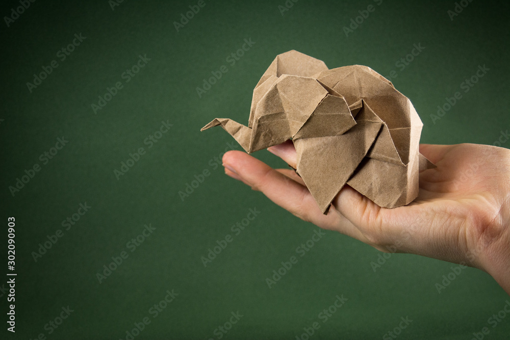 origami baby elephant craft paper on a green background on the hand ...