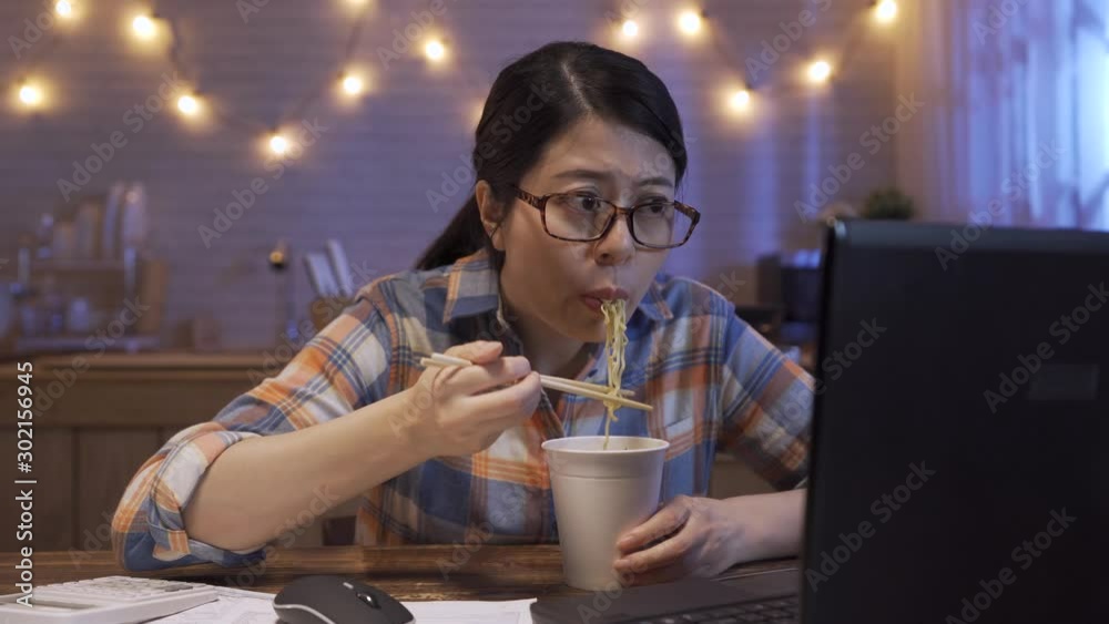 starving young asian japanese woman worker eating instant noodles while ...