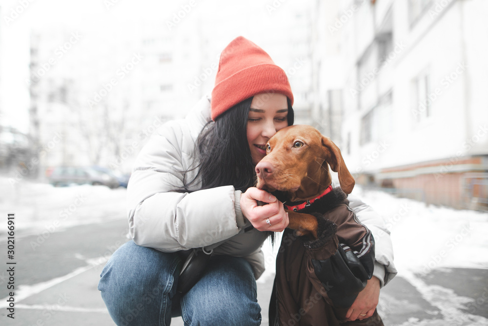 Happy girl hugs and kisses a beautiful orange dog on the background of ...