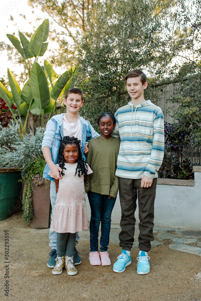 Smiling mixed-race siblings hugging near lush plants Stock Photo ...