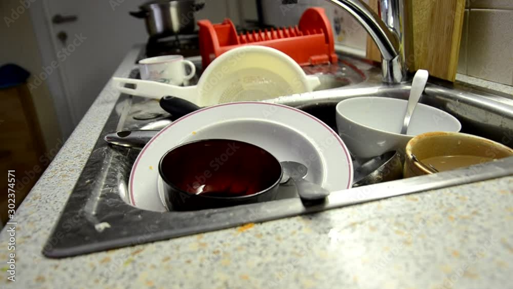 Woman hands rinse plate at the kitchen sink - doing the chores at home ...