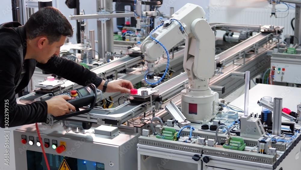 industry 4.0 concept: Man (engineer) is holding product and teaching robotic arm the points with ...