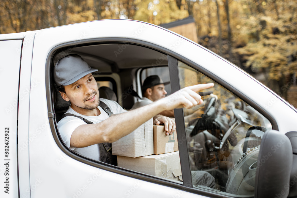 Delivery company employees driving cargo vehicle, delivering goods to ...