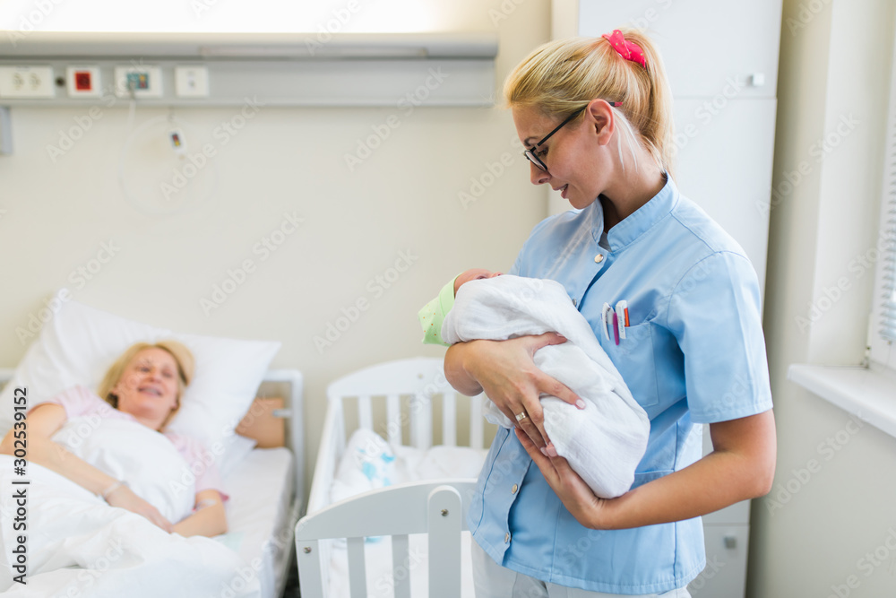 Young nurse standing in maternity ward and holding newborn baby in her ...