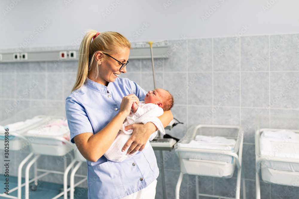 Young nurse standing in maternity ward and holding newborn baby in her ...