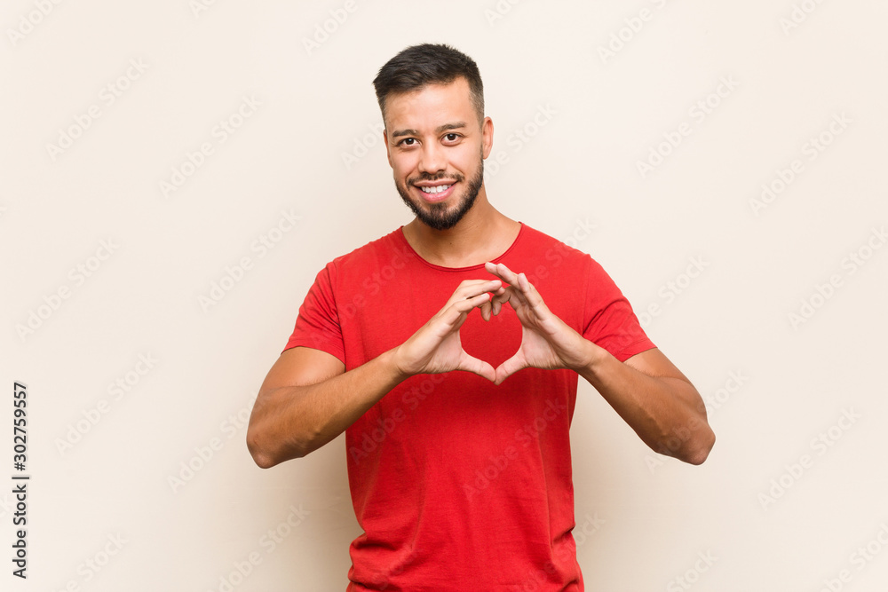 Young south-asian man smiling and showing a heart shape with hands ...