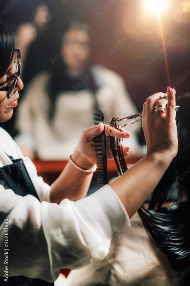 Woman getting a new haircut. Female hairstylist cutting her long black ...