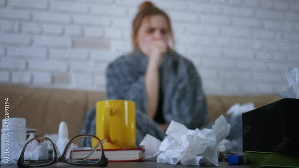 Attractive ill caucasian girl wearing grey blanket sitting on sofa in ...