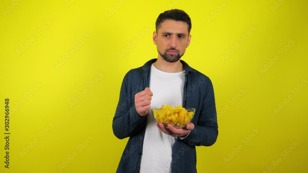 Young man in blue shirt and white T-shirt is eats not tasty chips from ...