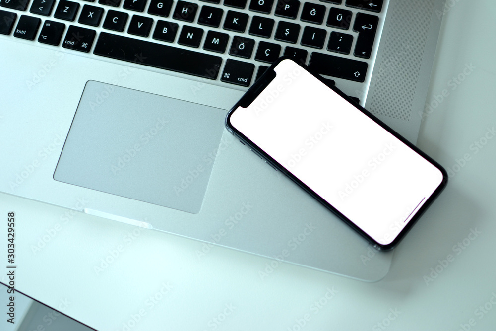 There is an Apple iPhone XS on a MacBook Pro on the office desk. It is ...