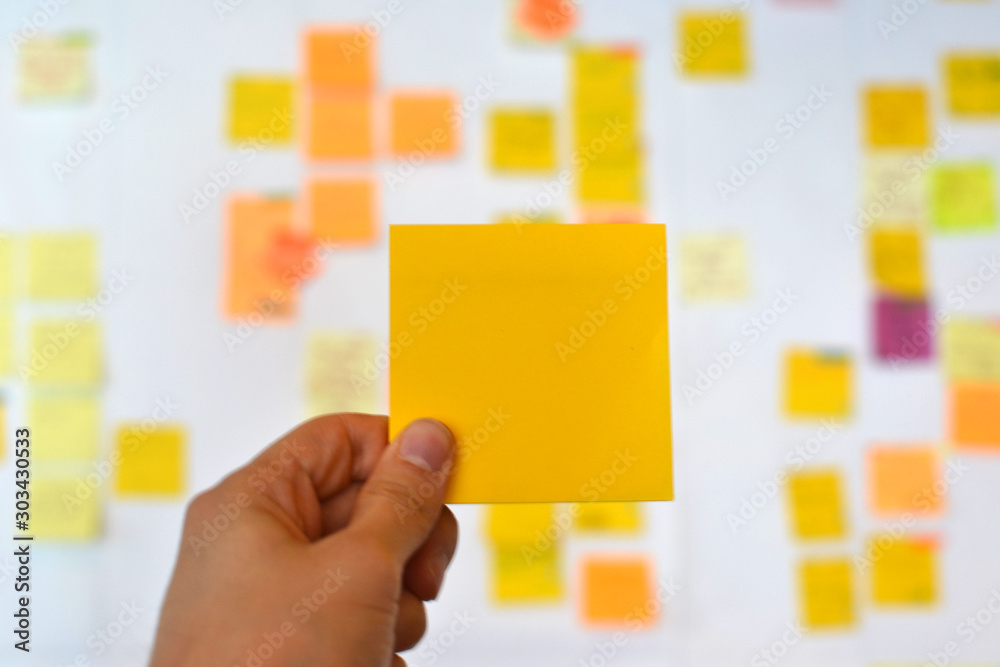 A hand is holding a orange blank sticker and there is a Kanban board of ...