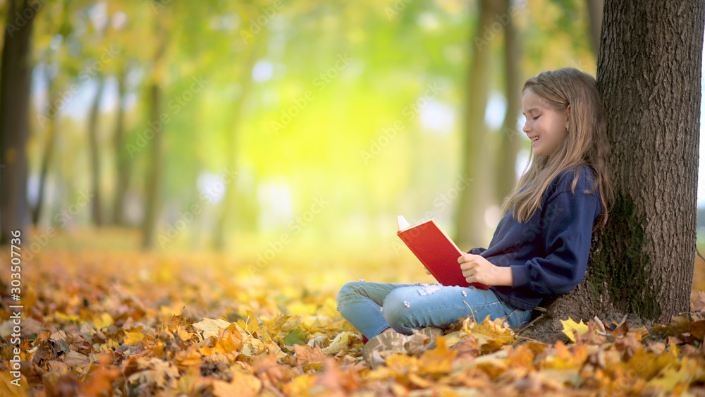 cute girl sitting under a tree in the park and reading a book ...