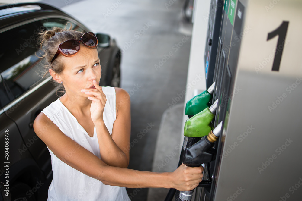 Young woman pumping gas at gas pump. Soaring gas prices concept. Fossil ...
