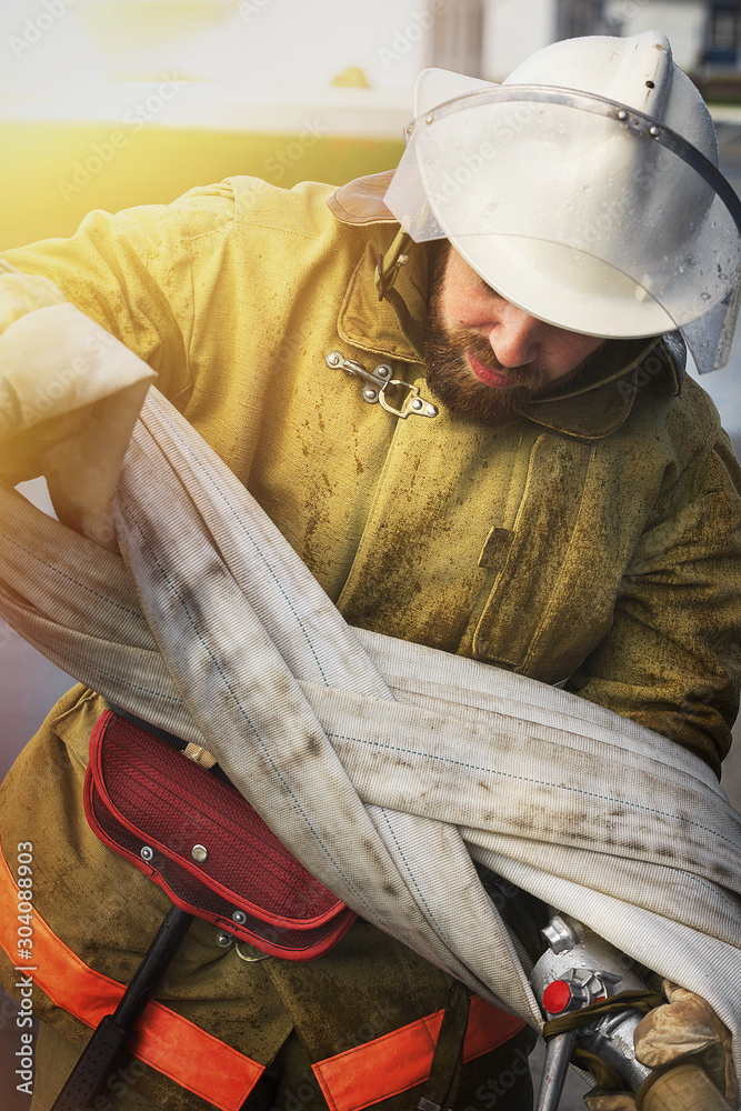 A bearded fireman in a helmet and overalls twists a fire hose. End of ...