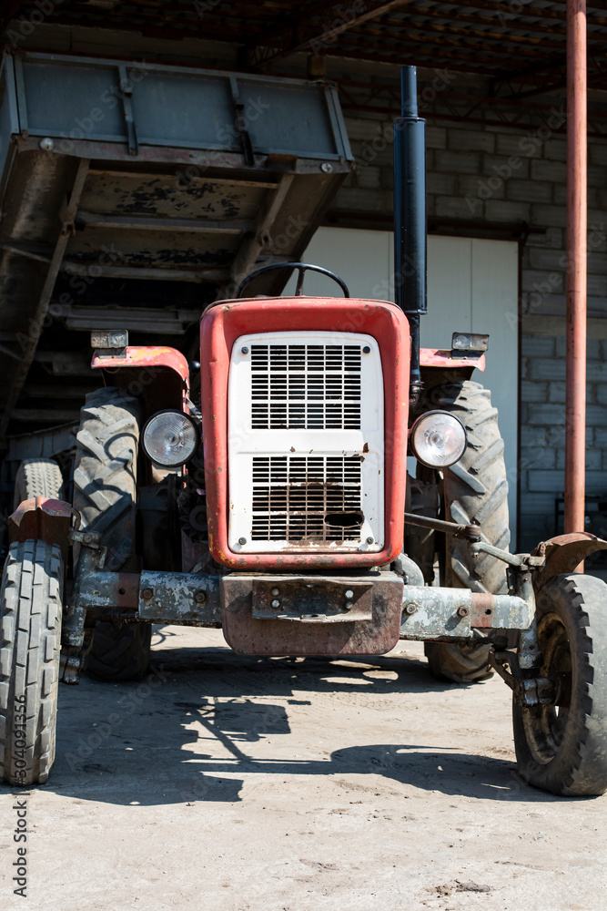 Old red farm tractor with an agricultural trailer, front view. Works on ...
