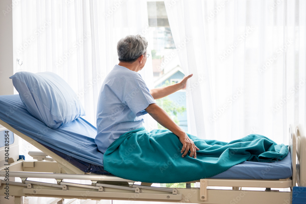 Asian patient man looking outside and sitting on hospital bed in the ...