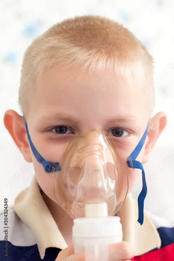 Sick boy inhaling through inhaler mask, face close-up view. Use ...