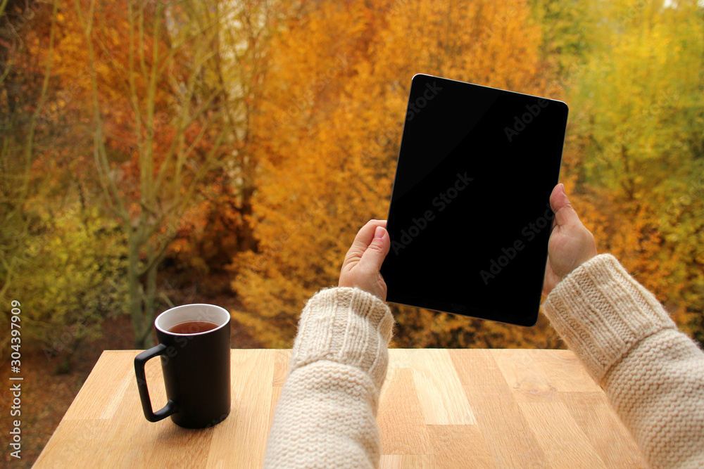 girl holds upright tablet PC with pre-keyed black screen, mug with tea ...