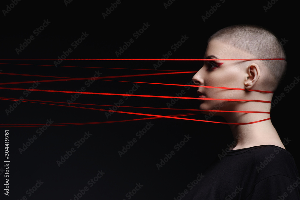 Side view of young beautiful woman with red threads around head on dark ...
