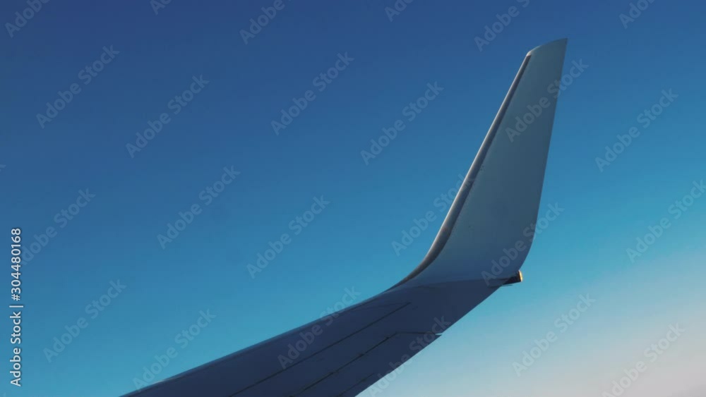 Plane is flying against of a clean blue sky background. View white wing ...