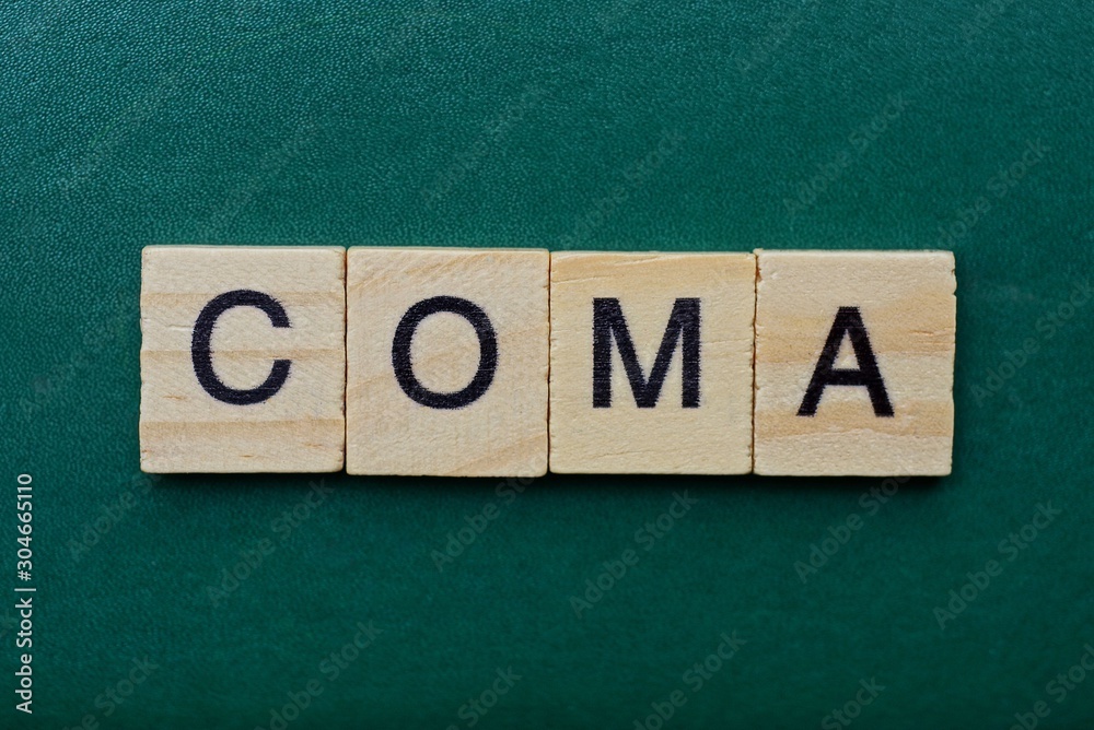 word coma made from gray wooden letters lies on a green background ...