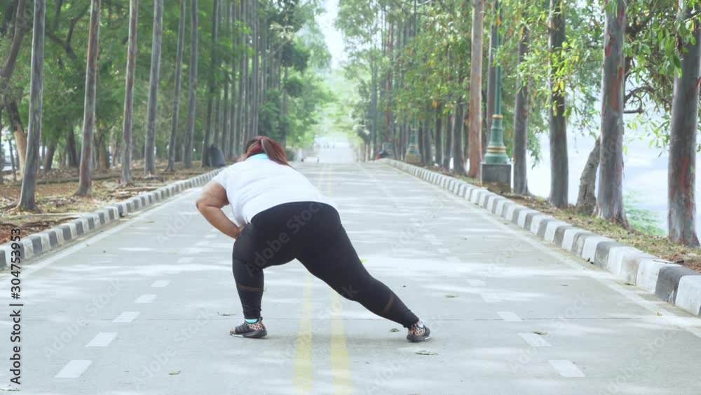 Rear view of obese woman doing stretching exercises on the road while ...