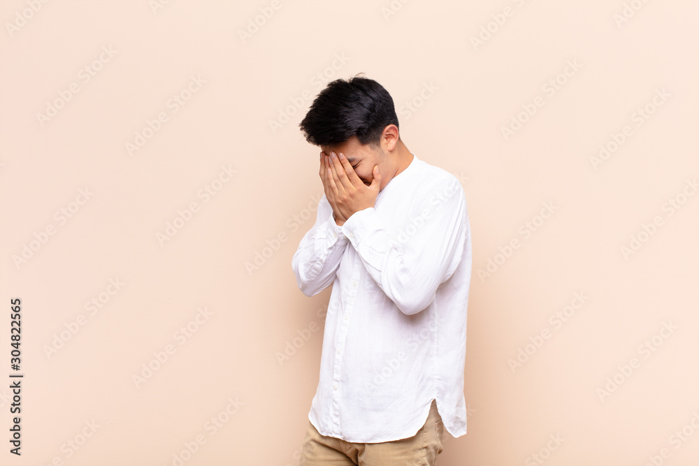 young chinese man covering eyes with hands with a sad, frustrated look ...