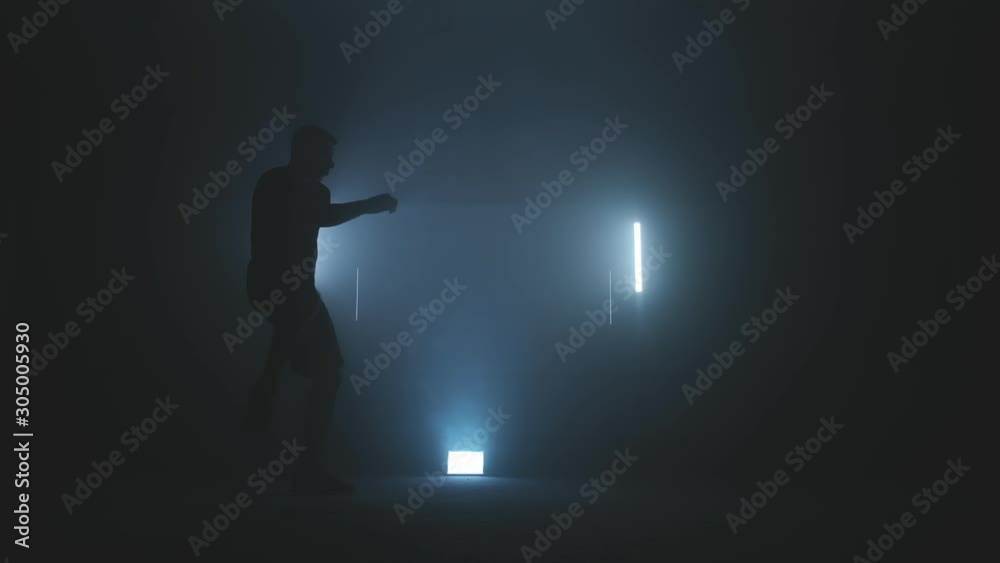 Strong athlete hit with leg jumping in gym. Kickboxer training in dark ...