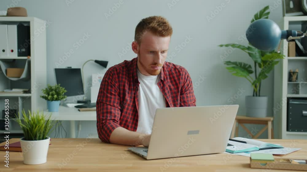 Tired ginger-haired guy employee is working with computer in office ...