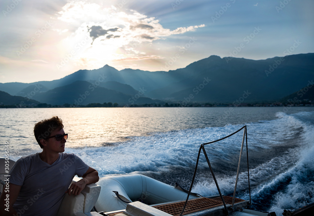 Young man sitting on landing deck on the back of luxury motorboat with ...