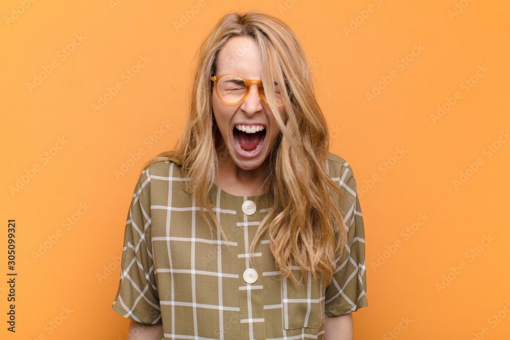 young pretty blonde woman shouting aggressively, looking very angry ...