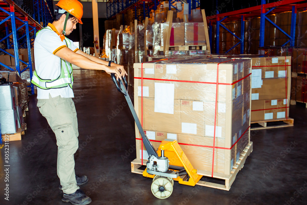 Warehouse worker with hand pallet truck unloading heavy shipment goods ...