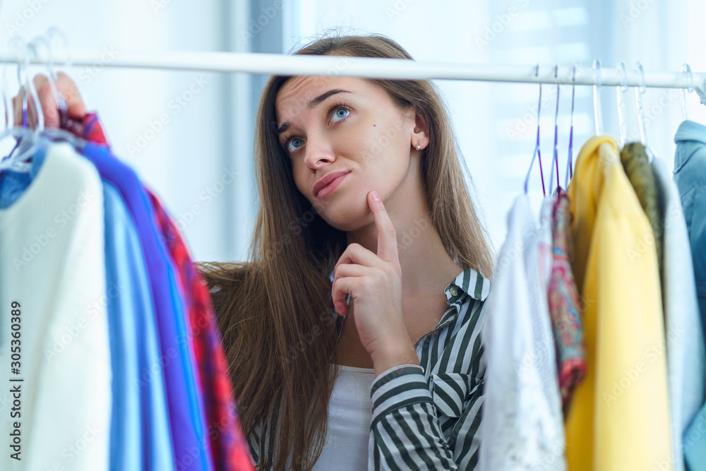 Woman standing near wardrobe rack full of clothes on hangers, having ...