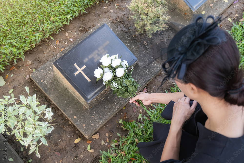 Mourning young woman laying white flowers on her family grave in ...