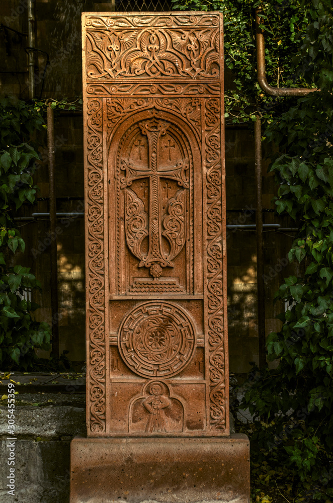 A red tuff khachkar with a floral pattern over an arch with a cross,a ...