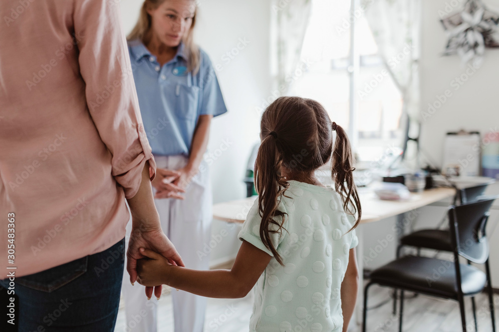 Girl holding hands of mother while female pediatrician explaining in ...