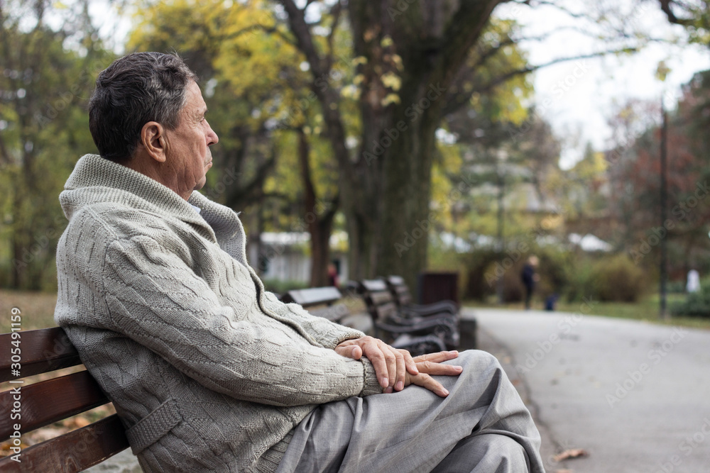 Portrait of a pensive senior man sitting on the bench, in the public ...