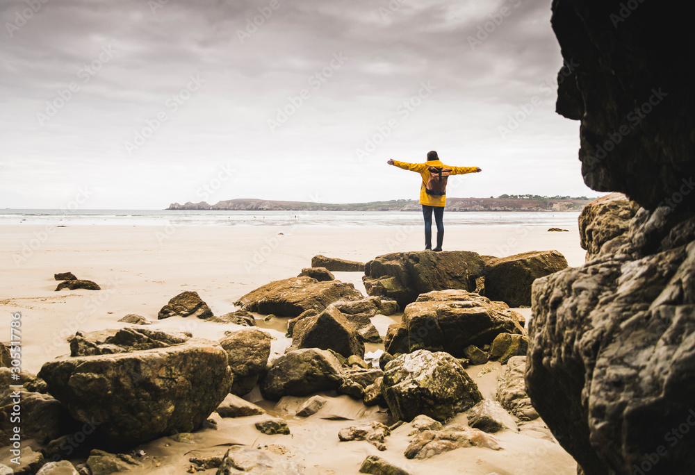 Young woman wearing yellow rain jacket at the beach at rock cave ...