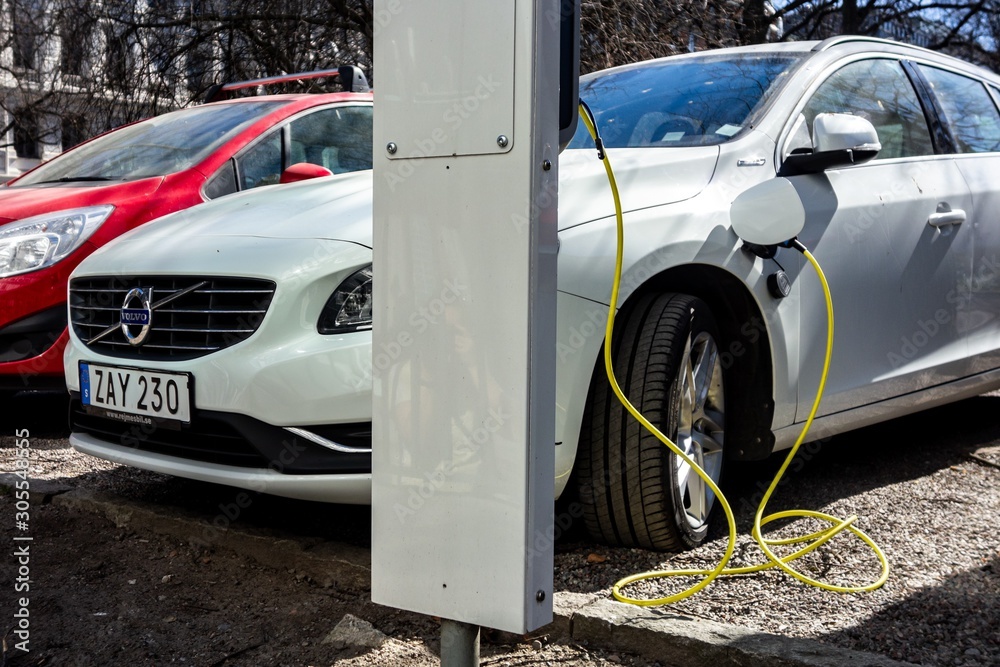 White modern plug-in Volvo car plugged and charging its battery with ...