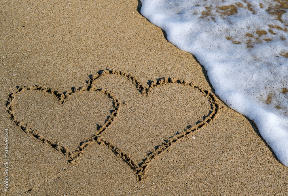 Hand drawn two Hearts on golden sand on beach. Drawing in sand for ...