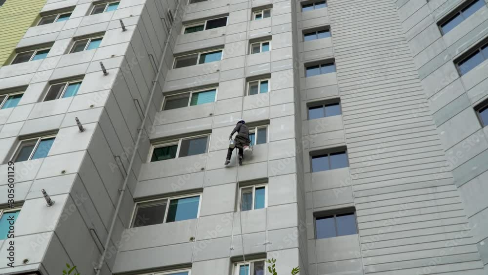 A maintenance worker is patching and painting a wall while suspended on ...