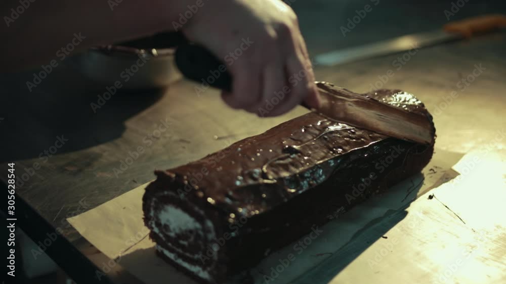 Hand with spatula is spreading chocolate on cocoa creamy swiss roll ...
