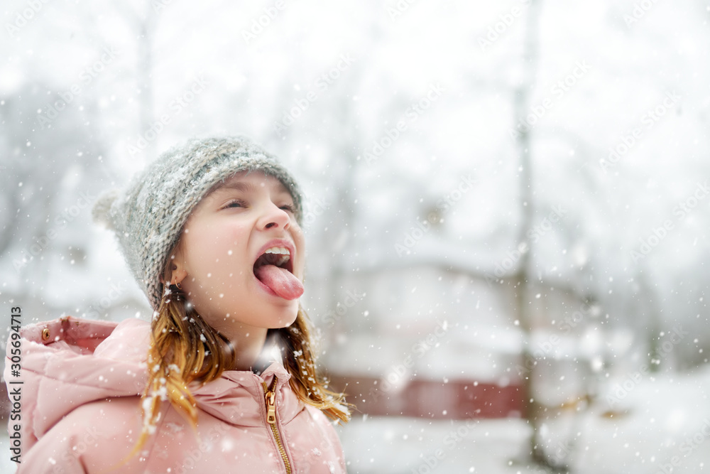 Adorable young girl catching snowflakes with her tongue in beautiful ...