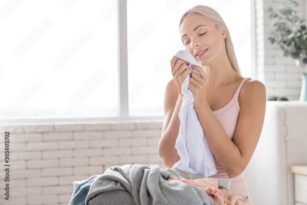 Beautiful young woman smelling clean clothes and smiling while doing ...