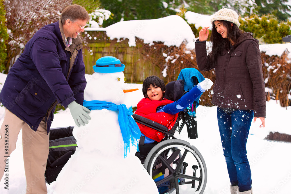 Disabled boy in wheelchair building snowman with family during winter ...
