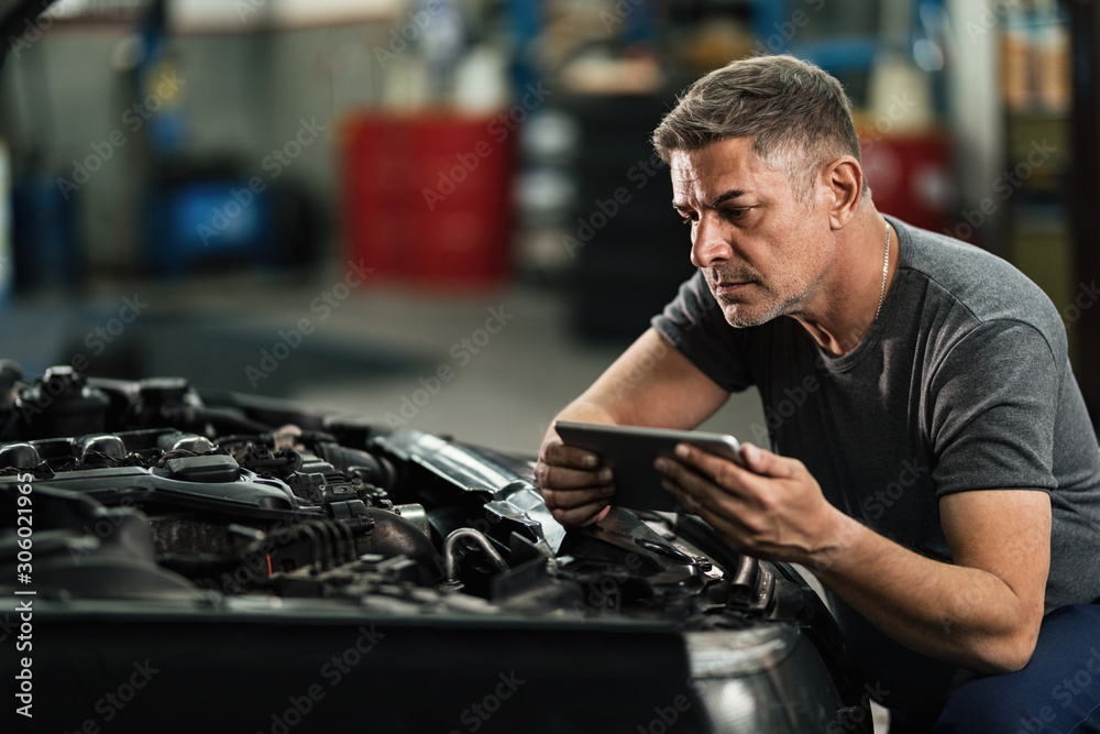 Auto mechanic using touchpad while examining car engine in a workshop ...