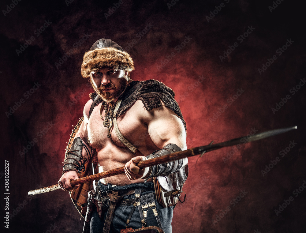 Serious Viking clad in light armor with a shield behind his back holds ...