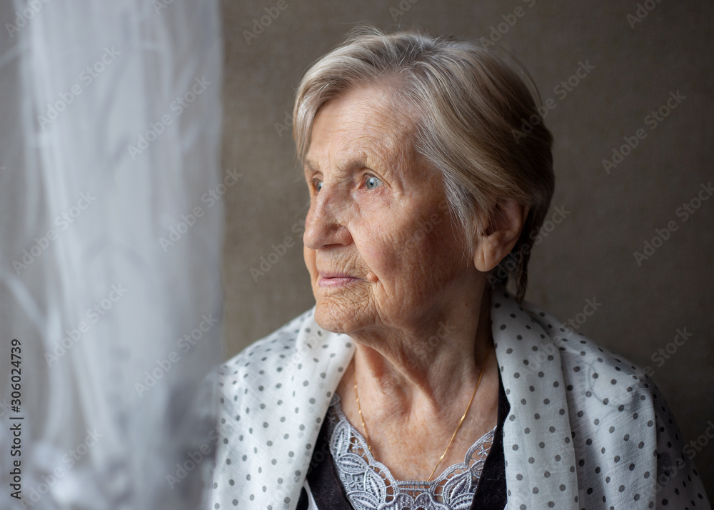 Old woman looks out window, sad, remembers, thinks. Closeup portrait ...